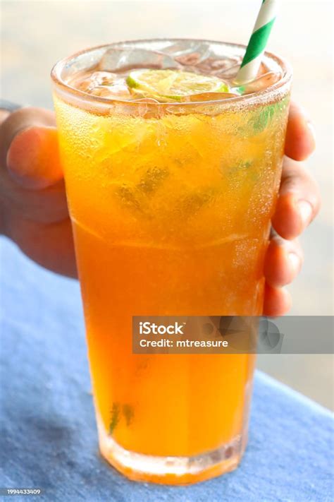 해변 레스토랑 바 장면의 클로즈업 이미지 녹색과 흰색 종이로 감귤류 오렌지 목테일을 들고 있는 알아볼 수 없는 사람 빨대 파란색 식탁보가 있는 테이블에 얼음 조각과 라임
