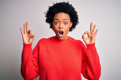 젊은 아름 다운 아프리카 계 미국인 Afro 여자 곱슬 머리 빨간 캐주얼 스웨터를 입고 보고 놀라 고 손가락으로 확인 승인