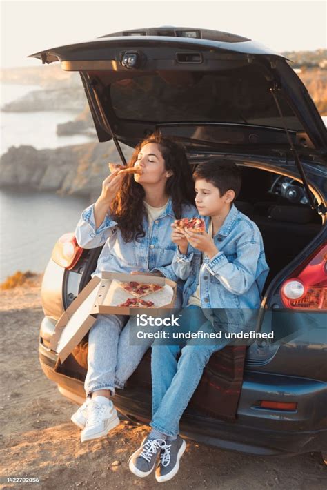 전신 어머니와 십대 아들은 자동차 트렁크에 앉아서 상자에서 피자를 가져 오는 조각을 먹습니다 가족 휴가 여행 차에 대한 스톡