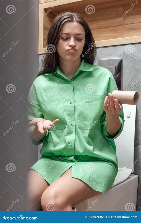Young Woman Sitting On A Toilet Holding Stomach Stock