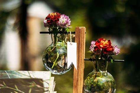 금잔화와 보라색 꽃을 포함한 여름 꽃이 있는 유리 꽃병이 나무 구조물 위에 놓여 있습니다 꽃병에 물방울이 보입니다 꽃병에는 빈