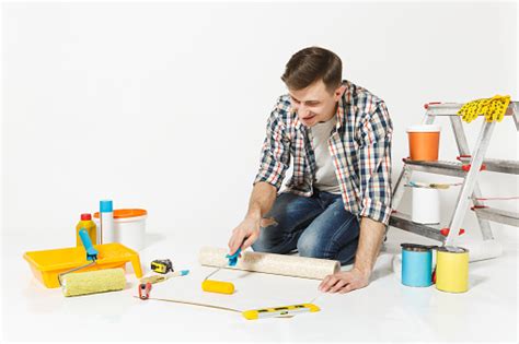 젊은 남자 벽지 롤 페인트 롤러 흰색 배경에 고립 된 재건축 아파트 룸에 대 한 악기와 함께 바닥에 앉아 벽지 액세서리를 붙이기 그림 도구 수리 홈 개념 개선에 대한 스톡