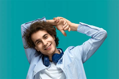 얼굴을 찡그리다 흰색 티셔츠와 파란색 셔츠를 입은 젊은 아름다운 남자의 초상화가 머리 뒤에 손을 잡고 카메라를 바라보고 있습니다 20 29세에 대한 스톡 사진 및 기타