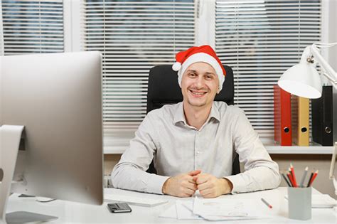 잘생긴 웃는 비즈니스 남자 셔츠와 빨간 크리스마스 모자는 책상에 앉아에 현대 모니터 빛 사무실에서 문서 창 배경에 카메라 보고 컴퓨터에서 작업 개미에 대한 스톡 사진 및