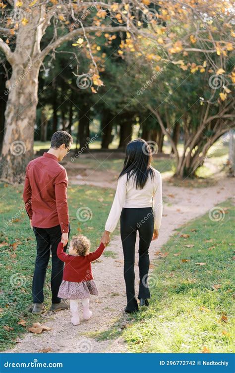 родители с маленькой девочкой идут по тропинке в парке держась за руки задний вид Стоковое