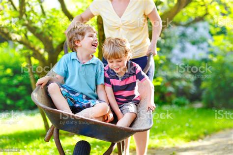 따뜻한 화창한 날에 국내 정원에서 어머니에 의해 추진 수레에 재미 두 작은 아이 소년 여름에 아이 들을 위한 활동적인 야외 게임 재미 형제와 함께 연주 최고의 친구 2명에