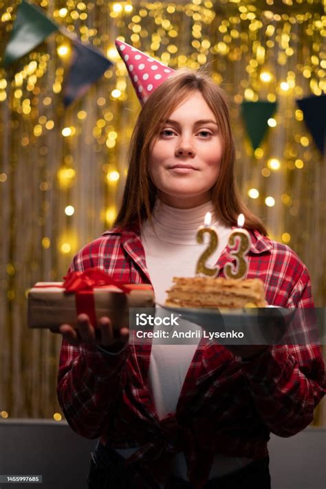 생일 축하 파티 모자를 쓴 소녀가 23번 촛불과 생일 선물이 있는 케이크를 들고 카메라를 보고 있다 18 19세에 대한 스톡 사진 및 기타 이미지 Istock