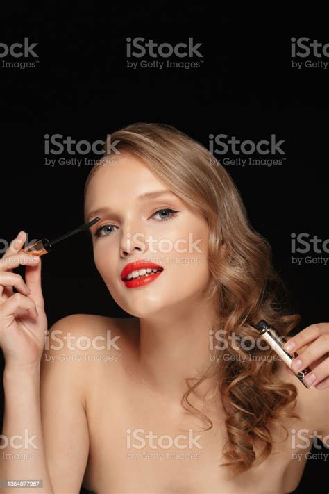 물결 모양의 머리와 빨간 입술을 들고 있는 젊은 아름다운 여성의 초상화가 검은 색 배경을 통해 카메라를 꿈꾸며 바라보며