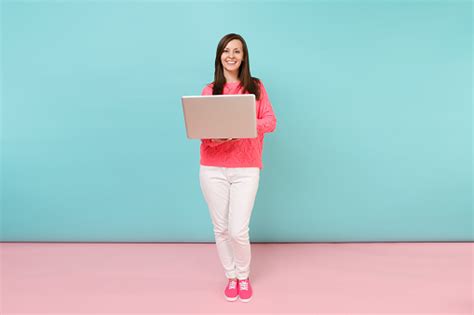 니트 장미 스웨터 스튜디오에서 밝은 분홍색 파란색 파스텔 벽 배경에 고립 된 노트북 Pc 컴퓨터를 사용 하 여 흰색 바지에서 여자의 전체 길이 초상화 패션 라이프 스타일