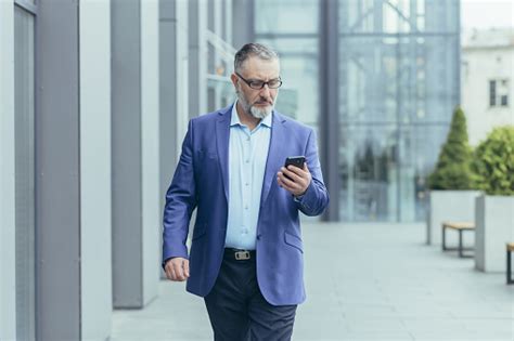 정장을 입은 사업가가 길거리의 사무실 센터 근처에서 걷고 휴대 전화를 들고 메시지를 입력하는 45 49세에 대한 스톡 사진 및 기타 이미지 Istock