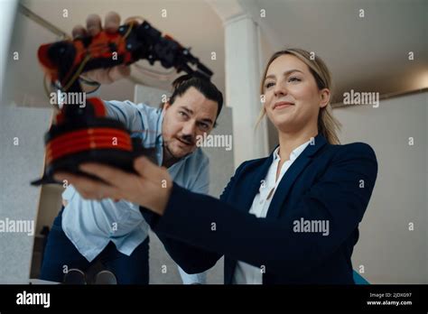 Engineer Discussing With Colleague Over Robotic Arm Model In Office
