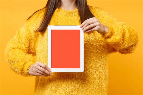 밝은 노란색 배경에 고립 된 빈 검은색 빈 화면으로 태블릿 Pc 컴퓨터를 들고 모피 스웨터에 젊은 갈색 머리 여자의 자른된