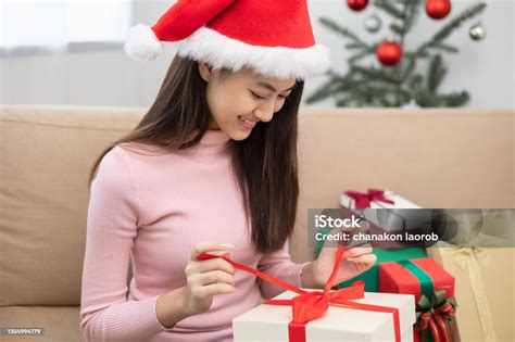 아름다운 아시아 여성은 상자 안에 무엇을 추측 선물 상자 풀 리본을 풀 포장을 풀 어린 행복한 귀여운 소녀는 집에서 소파에 앉아 많은 선물 상자와 크리스마스 휴가 축제에서