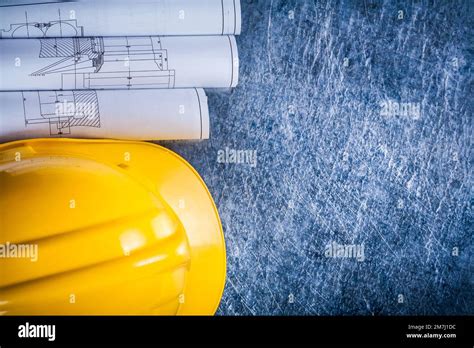 Set Of White Rolled Up Blueprints And Construction Helmet On Metallic Scratched Background