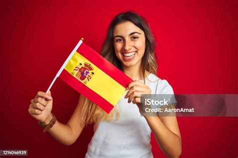 행복한 얼굴 서서 치아를 보여주는 자신감 미소와 함께 미소와 빨간색 고립 된 배경 위에 스페인어 깃발을 들고 젊은 아름다운 여자 스페인에 대한 스톡 사진 및 기타 이미지