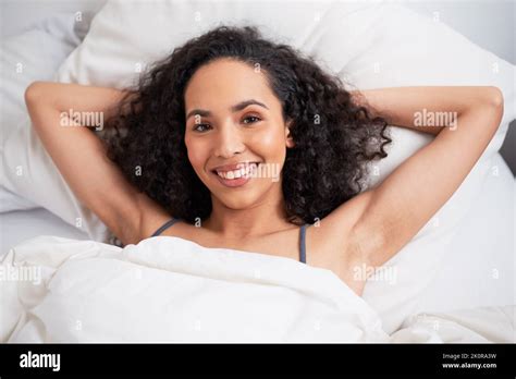 A Young Multi Ethnic Woman Lies With Arms Behind Head In Bed Smiling