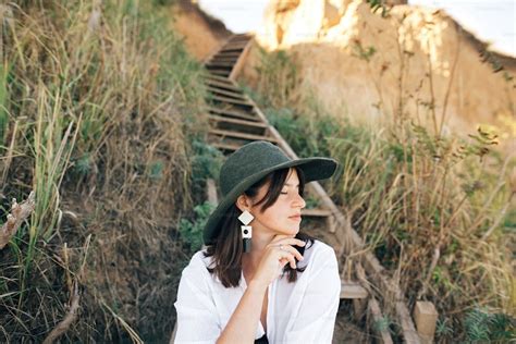 모자를 쓴 세련된 보헤미안 소녀는 바다 근처의 모래 절벽에서 햇살이 내리쬐는 나무 계단에 앉아 있다 열대 섬 해변에서 휴식을