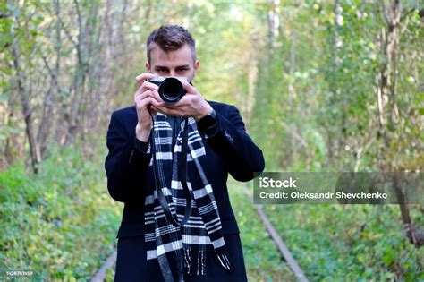 검은 코트와 스카프를 입고 직장에서 카메라가있는 사진 작가 가이는 카메라에서 사진을 찍습니다 코트와 스카프를 입은 사진 작가가 카메라를 향해 촬영합니다 남자 사업가에 대한