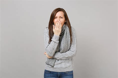 회색 스웨터 스카프 회색 벽 배경에 고립 종 려를 가진 덮 음 입 기침 또는 재채기에 젊은 여자 건강 한 생활 습관 병 아픈 질병 치료 추운 계절 개념 복사 공간을 비웃는