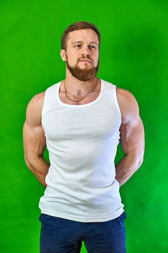 수염을 기고한 백인 남성이 흰색 티셔츠와 청바지를 입고 녹색 배경에 서 있다 전신 남자는 미소없이 멀리 보인다 캐주얼 스타일에