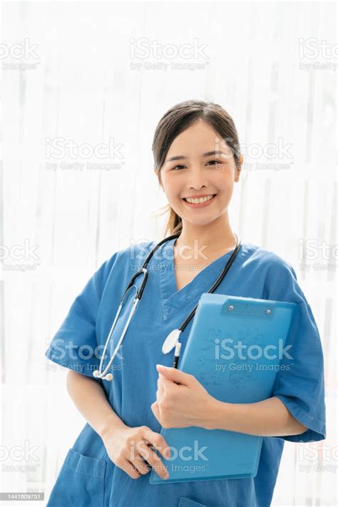 병원에서 카메라를 보고 웃고 있는 아시아 여성 또는 청진기가 서 있고 폴더를 들고 있는 파란색 의료 유니폼을 입은 여성 의사의 의료 개념 건강관리와 의술에 대한 스톡 사진