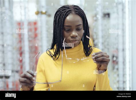 Young African Woman Choosing Between Two Prescription Glasses Frames In Opticians Shop Stock