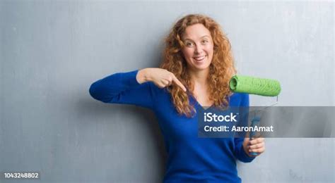 자신에 게 놀라운 얼굴 가리키는 손가락으로 그림 롤러를 들고 회색 그런 지 벽에 빨강 머리 젊은 여자 가리키기에 대한 스톡 사진 및 기타 이미지 Istock