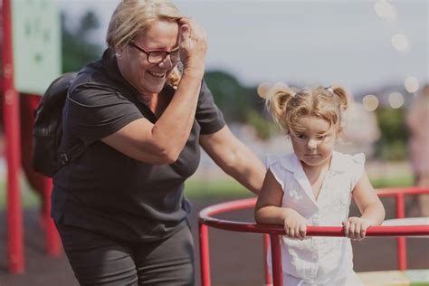 An Older Grandmother Is Playing With Her Grandson In The Park At Sunset