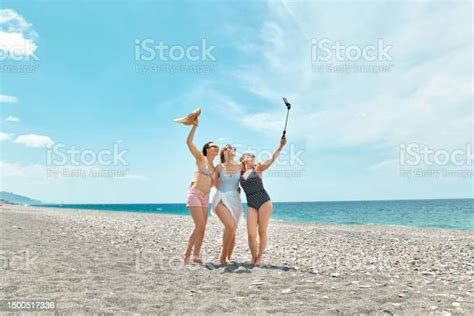 세 명의 여자 친구들이 해변을 걷고 셀카를 찍고 여름날 웃고 있다 쾌활한 여성들이 바다 근처에서 함께 여름 휴가를 즐기고 있다
