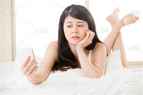 年轻的亚洲女性在床上使用智能手机阅读