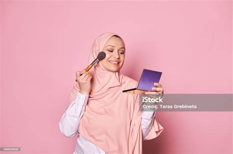 분홍색 히잡을 쓴 매력적인 중년 아랍 무슬림 여성 얼굴에 화장을 하고 분홍색 배경에 고립되어 있다 가정 생활에 대한 스톡 사진 및 기타 이미지 Istock