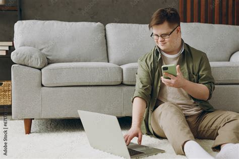 Young Man With Down Syndrome Wear Casual Clothes Use Laptop Pc Computer Mobile Cell Phone Sit