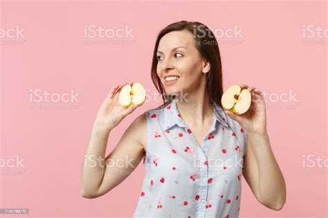 여름 옷에 아름 다운 젊은 여자 분홍색 파스텔 배경에 고립 된 신선한 잘 익은 사과 과일의 Halfs를 들고 옆으로 찾고 사람들은 생생한 라이프 스타일 휴식 휴가 개념입니다