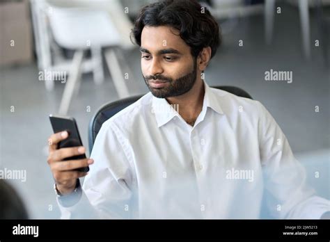 Young Indian Businessman Using Mobile Phone Apps At Work In Office