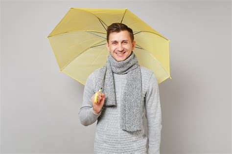 회색 스웨터에 젊은 남자를 웃 고 회색 배경 스튜디오 초상화에 격리 하는 노란 우산을 들고 스카프 건강 패션 라이프 스타일 사람들이 진심으 감정 추운 계절 개념 복사 공간을