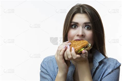 不健康的饮食概念。吃汉堡的白人女人。在室内工作室里穿着条纹衬衫摆姿势。水平射