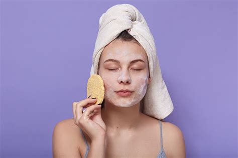 그녀의 얼굴 근처 스폰지와 머리에 흰색 수건에 여자의 수평 샷 눈을 감고 유지 스킨 케어 클렌징 화장품 스파 편안한 개념 아침에