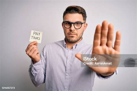 진지하고 자신감있는 표정 방어 제스처로 정지 표지판을하는 열린 손으로 종이 메모에 세금 단어를 들고 파란 눈을 가진 젊은 사업가 경계 표지에 대한 스톡 사진 및 기타 이미지