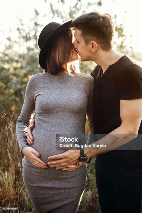 행복 한 젊은 부모 엄마와 아빠 아기 범프를 포옹 키스 일몰에 아름 다운 순간을 즐기고 부모의 개념입니다 세련 된 임신한 커플가을 공원에서 화창한 빛에 배를 잡고 손을 들고