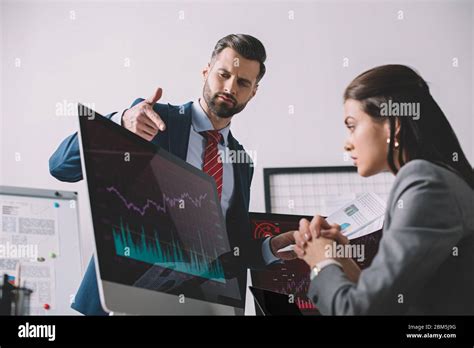 selective focus of data analyst with papers pointing on graphs on computer monitor to colleague