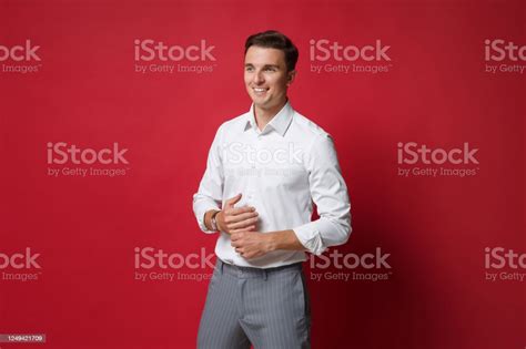 흰색 셔츠를 입은 젊은 사업가 밝은 빨간 벽 배경 스튜디오 초상화에 고립 된 포즈를 취하는 회색 바지 성취 경력 재산 사업 개념 복사 공간을 모의합니다 옆으로 찾고 유색