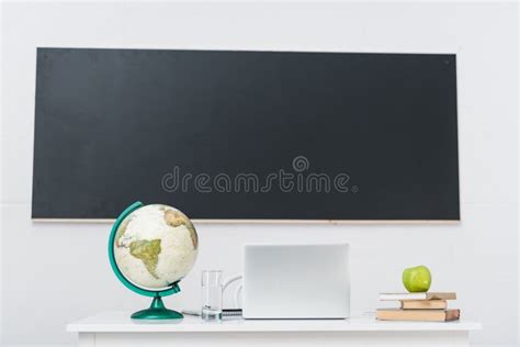 Teachers Desk With Laptop In Classroom In Front Of Chalkboard Stock