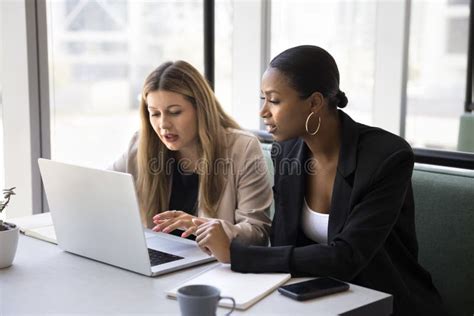 Two Focused Serious Multiethnic Female Business Colleagues Discussing Project Stock Image
