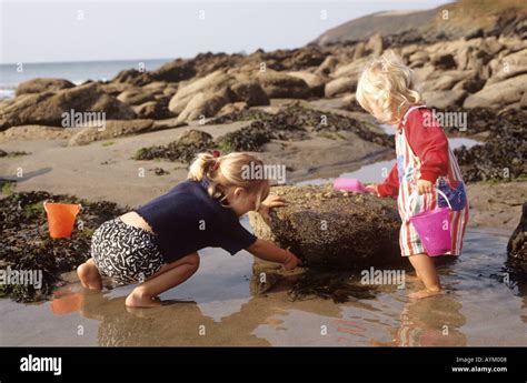 Young Girls Playing In A Rock Pool Together On A Beach In Cornwall In