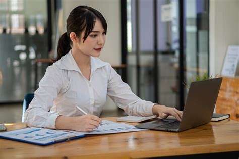 비즈니스 보고서 및 회계 계산기 개념으로 금융에 대해 사무실에서 노트북으로 작업하는 아름다운 아시아 여성 결과를 보여주는 차트