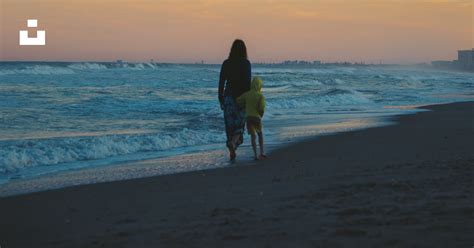 검은 재킷을 입은 여자가 일몰 동안 해변을 걷고 있습니다 사진 Unsplash의 무료 파랑 이미지