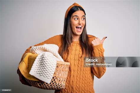 젊은 아름 다운 갈색 머리 여자 하 고 집안일 들고 고리버들 바구니 와 옷 가리키고 보여주는 엄지 손가락으로 옆구리와 행복한