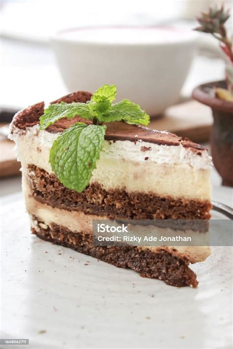 맛있는 티라미수 케이크는 코코아 가루와 민트 잎을 장식으로 얹은 전형적인 이탈리아 치즈 케이크로 포크가 달린 흰색 접시에