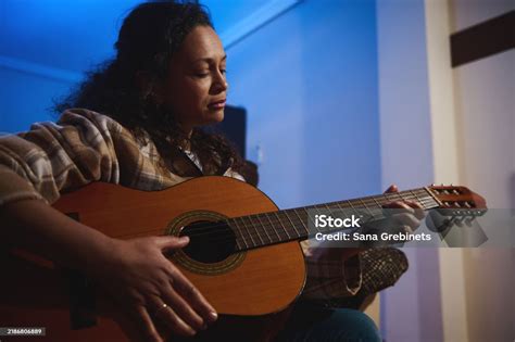 따뜻한 조명이 있는 아늑한 방에서 집에서 어쿠스틱 기타를 연주하는 여성 음악적 표현과 휴식의 고요하고 반사적인 분위기를 조성합니다 40 44세에 대한 스톡 사진 및 기타