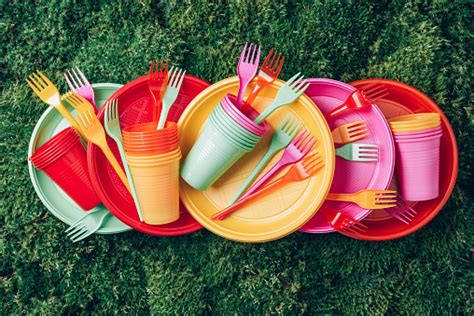 일회용 플라스틱 식기 접시 포크 숟가락 녹색 잔디 이끼 배경에 컬러 플라스틱 일회용 식기 맨 위 보기입니다 공간을 복사합니다 생일 피크닉 기구 플라스틱 및 생태 재활용